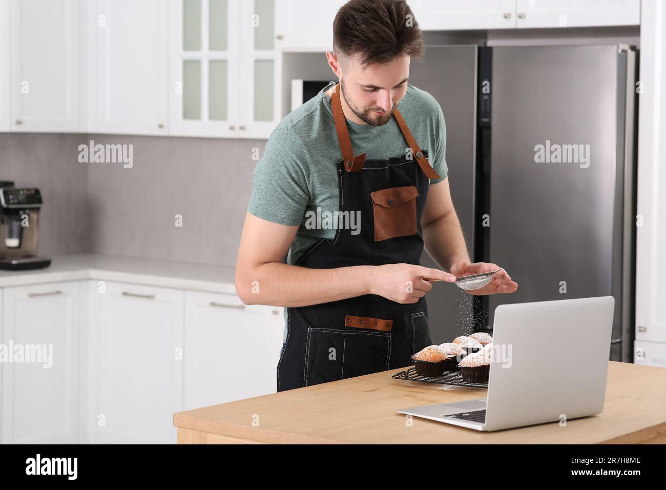 Homme décorant des muffins avec du sucre en poudre tout en regardant le ...