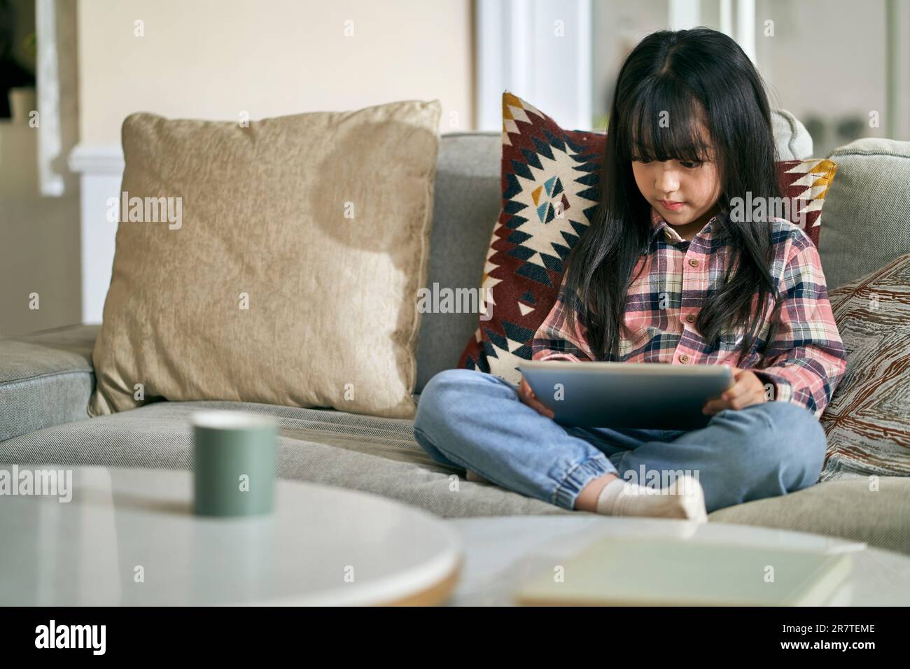 petite fille asiatique de sept ans assise sur un canapé de famille à la ...