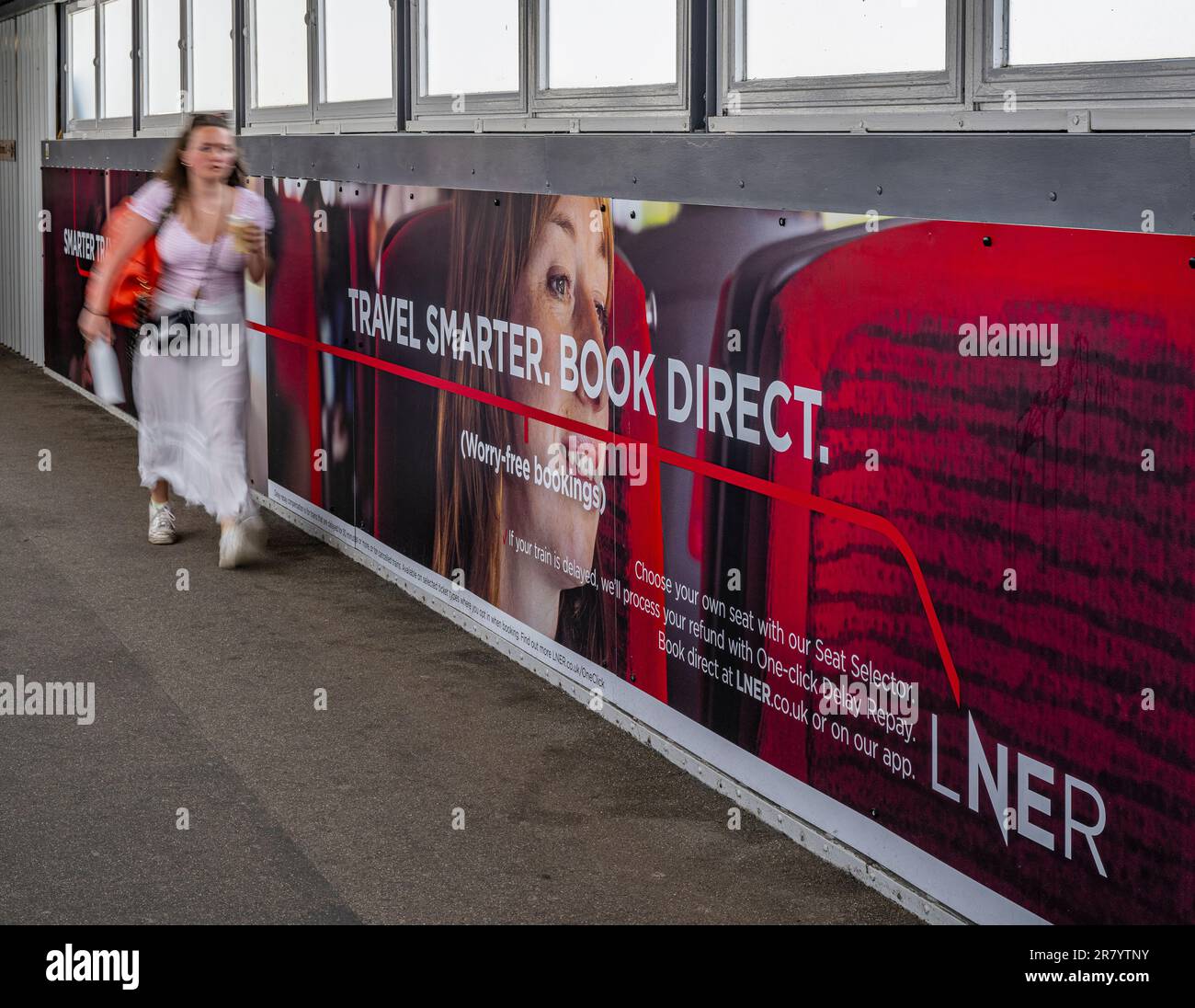 Une jeune femme marchant devant une palissade publicitaire pour le ...