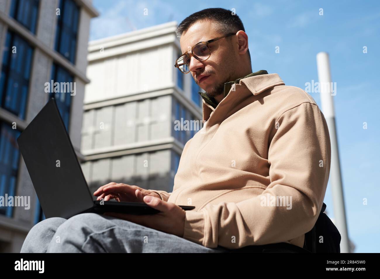 Vue à angle bas d'un jeune homme handicapé se concentrant sur son travail en ligne sur un ...