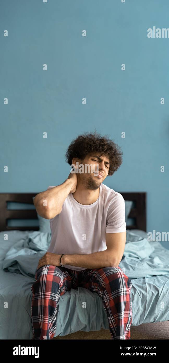 Douleur dans le cou. Homme attrayant assis sur le lit et tenant un cou ...