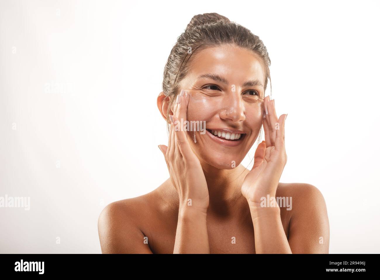 Belle fille fait sa routine de soin de peau tout en souriant et posant au studio sur un blanc ...