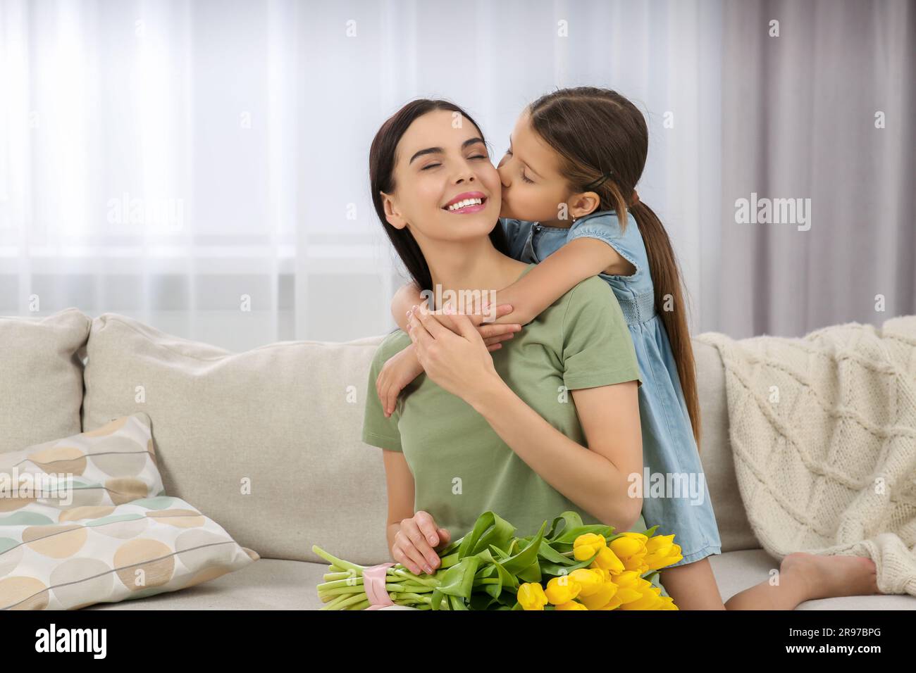 Femme heureuse avec sa fille et bouquet de tulipes jaunes sur le canapé ...