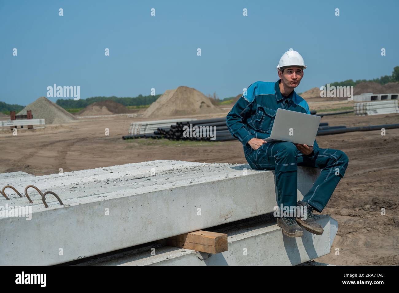 Le fabricant mâle caucasien en casque de chantier est assis sur des dalles de sol et utilise un ...