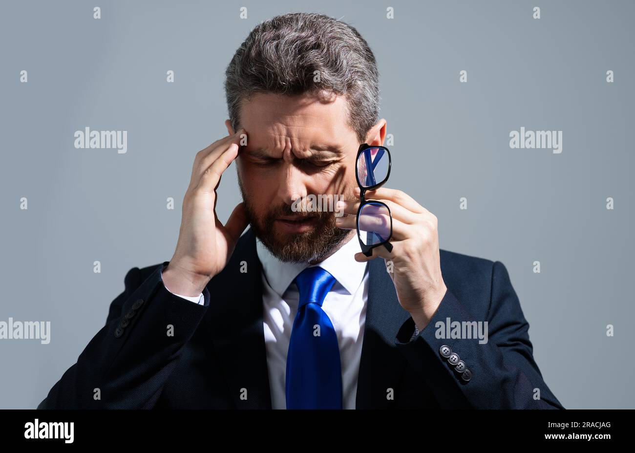 Homme avec mal de tête sur fond gris isolé de studio. L'homme ressent de la douleur se frottant ...