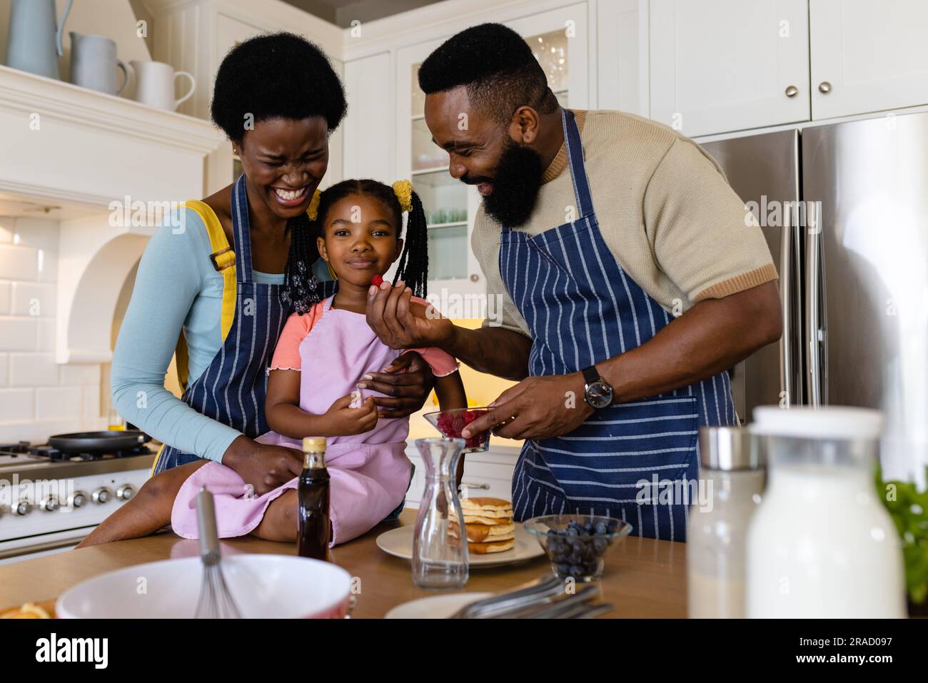 Joyeux homme afro-américain nourrissant des fruits à la fille tenue par la mère sur le comptoir ...