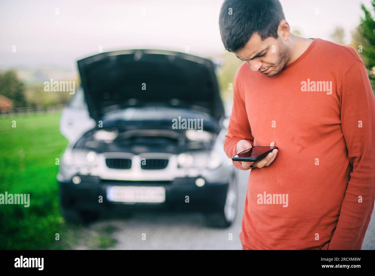 Un jeune conducteur a eu une panne de voiture sur la route. Il essaie ... Un jeune conducteur a eu une panne de voiture sur la route. Il essaie ...