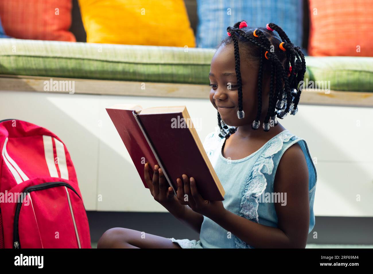 Heureuse écolière afro-américaine lisant un livre dans une salle ... Heureuse écolière afro-américaine lisant un livre dans une salle ...