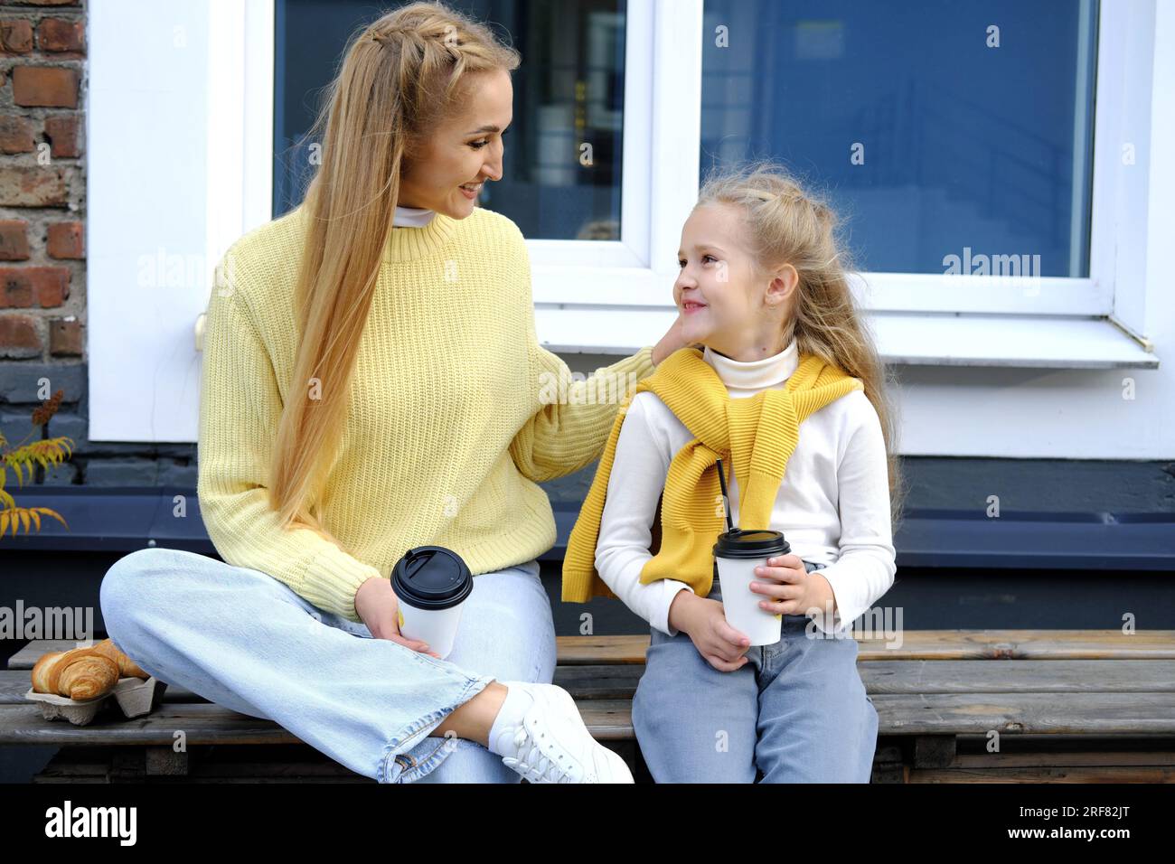 Maman et sa fille sont assises sur un banc avec des verres de chocolat ...