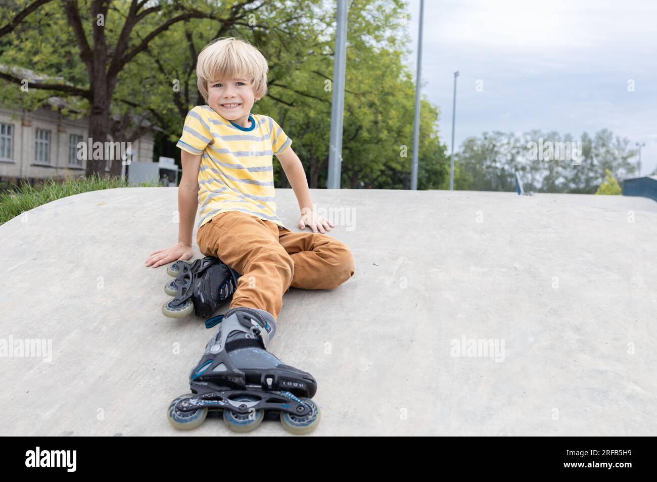 mignon garçon de 7 ans sur des patins à roulettes est assis sur le sol ...