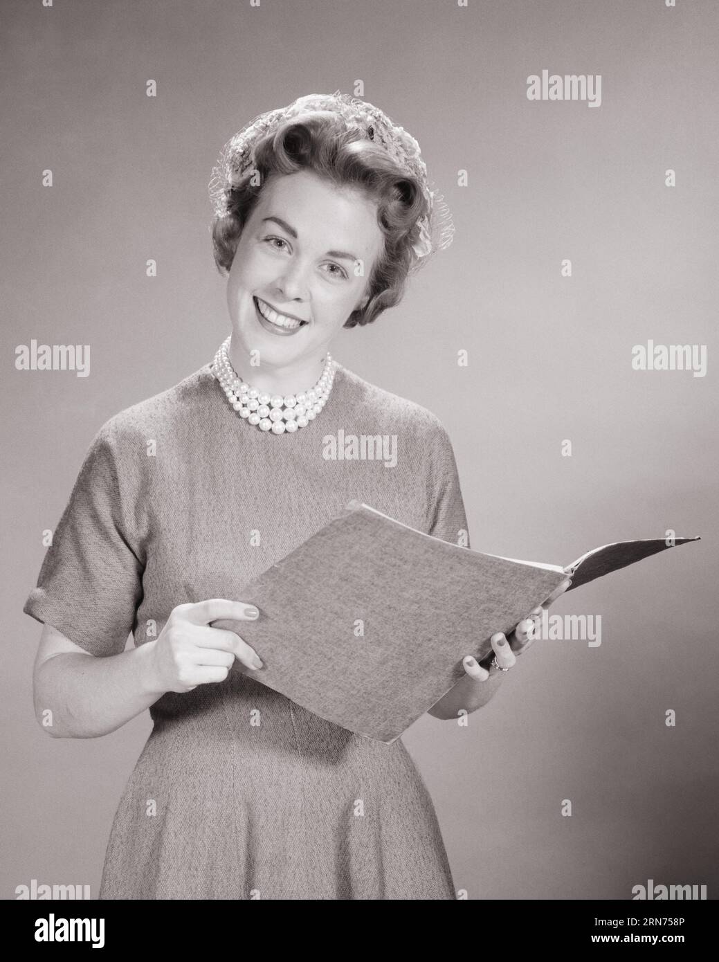 FEMME SOURIANTE DES ANNÉES 1960 LISANT À PARTIR DU DOSSIER PORTANT ...