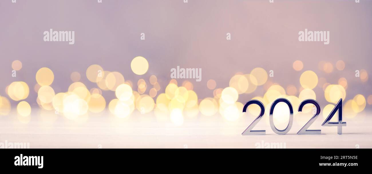 Numéros de métal 2024 sur une table blanche avec des arbres de Noël et des lumières de bokeh ...