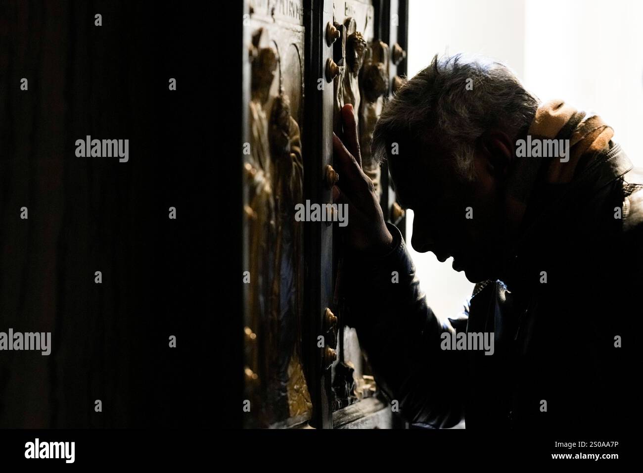 A man bows his head in prayer at the Holy Door of St.Peter's Basilica ...