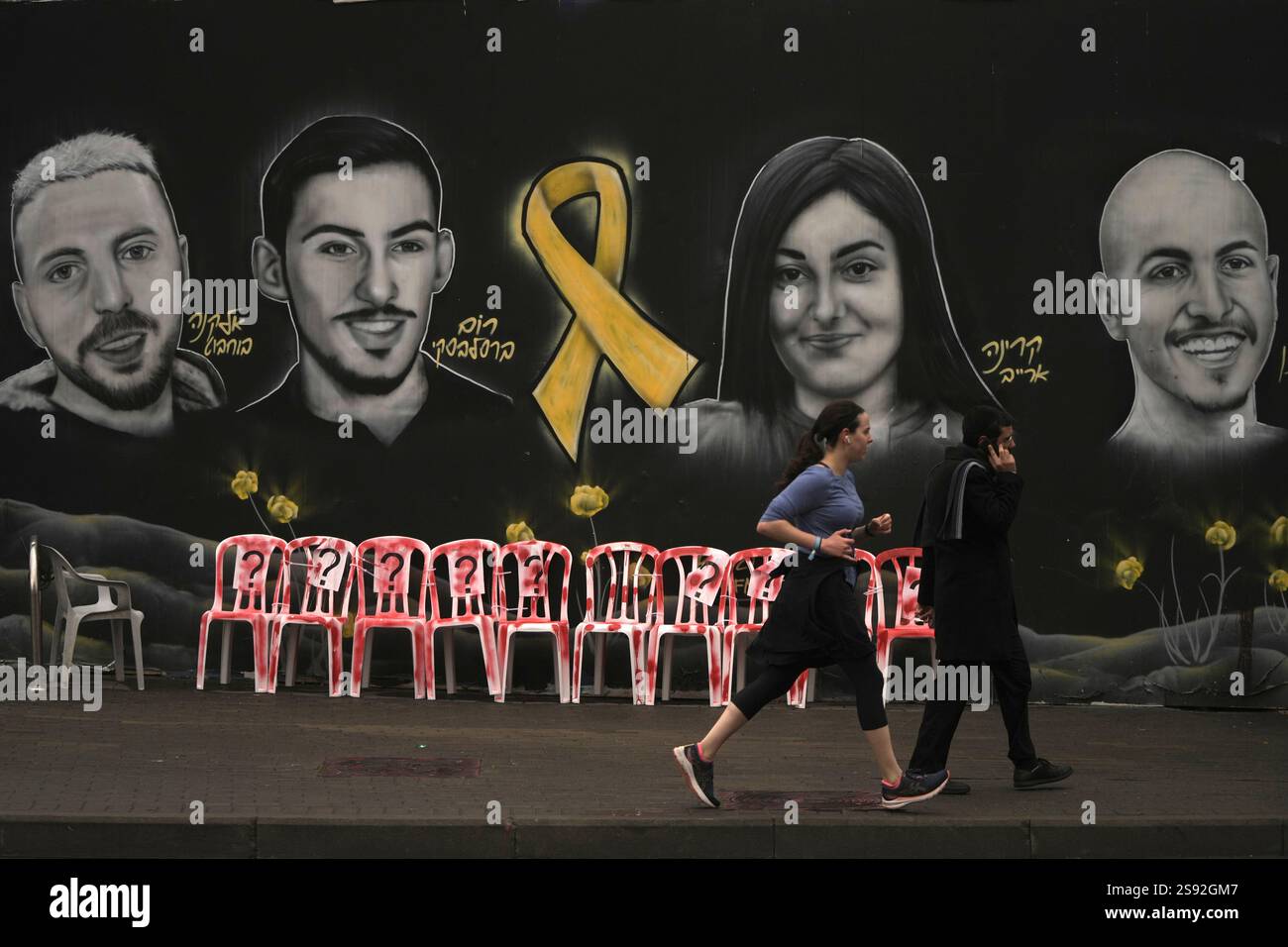 People walk and jog past an installation and a mural of portraits of ...