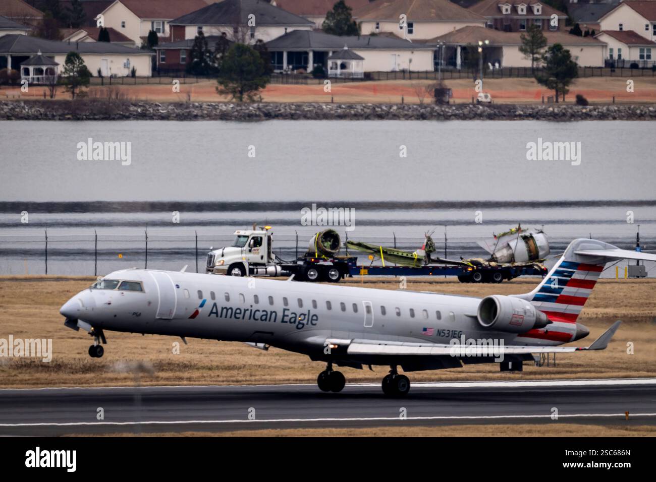 An aircraft lands on the runway as a flatbed truck carries away ...