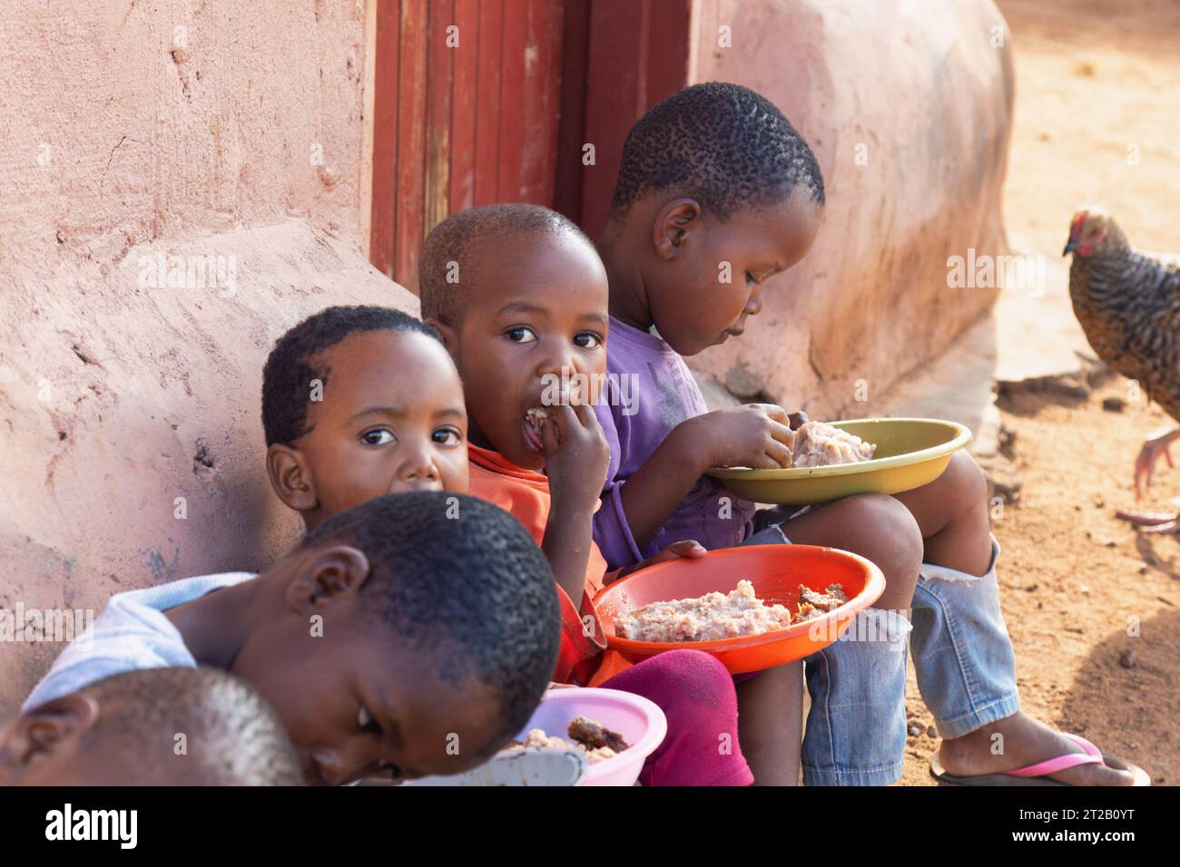Groupe d'enfants africains de village mangeant dans la cour, famine et ...