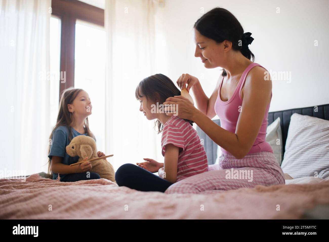 Mère avec deux filles sur un lit dans la chambre. Mère peigne les ...