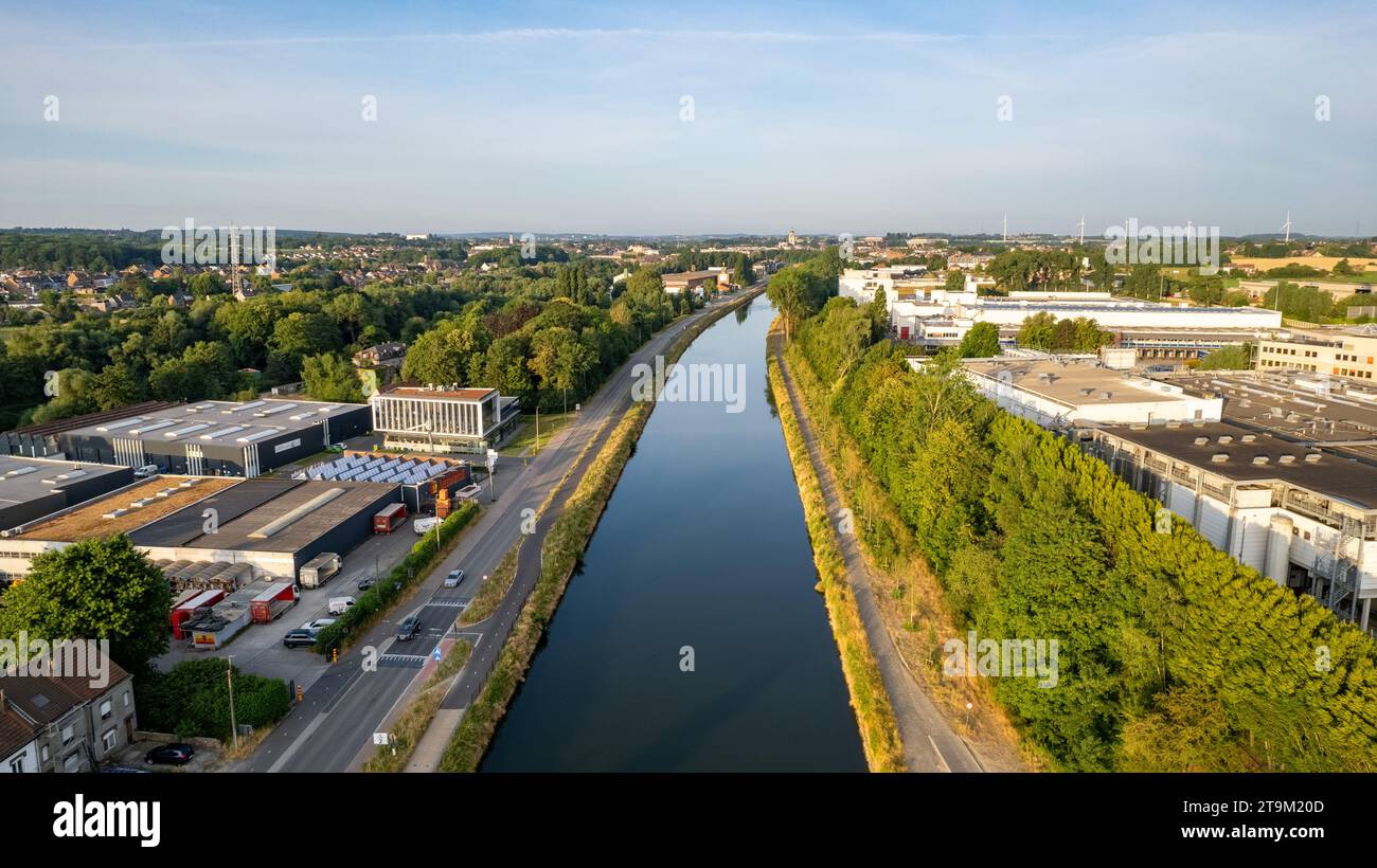 Cette image aérienne montre un canal serein traversant une zone urbaine, flanqué d’un côté par ...