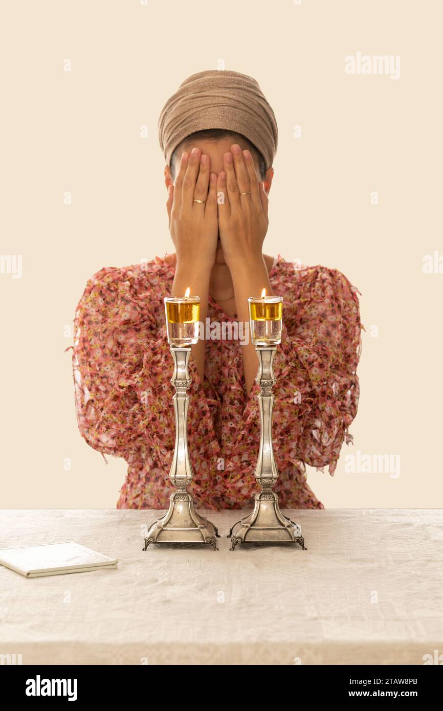 Femme juive prie sur des bougies de Shabbat allumées, couvrant son ...