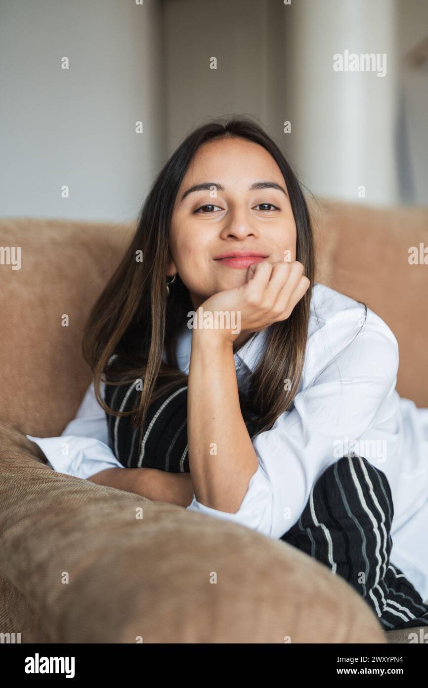Une jeune femme contente se prélasse sur un canapé, offrant un sourire ...