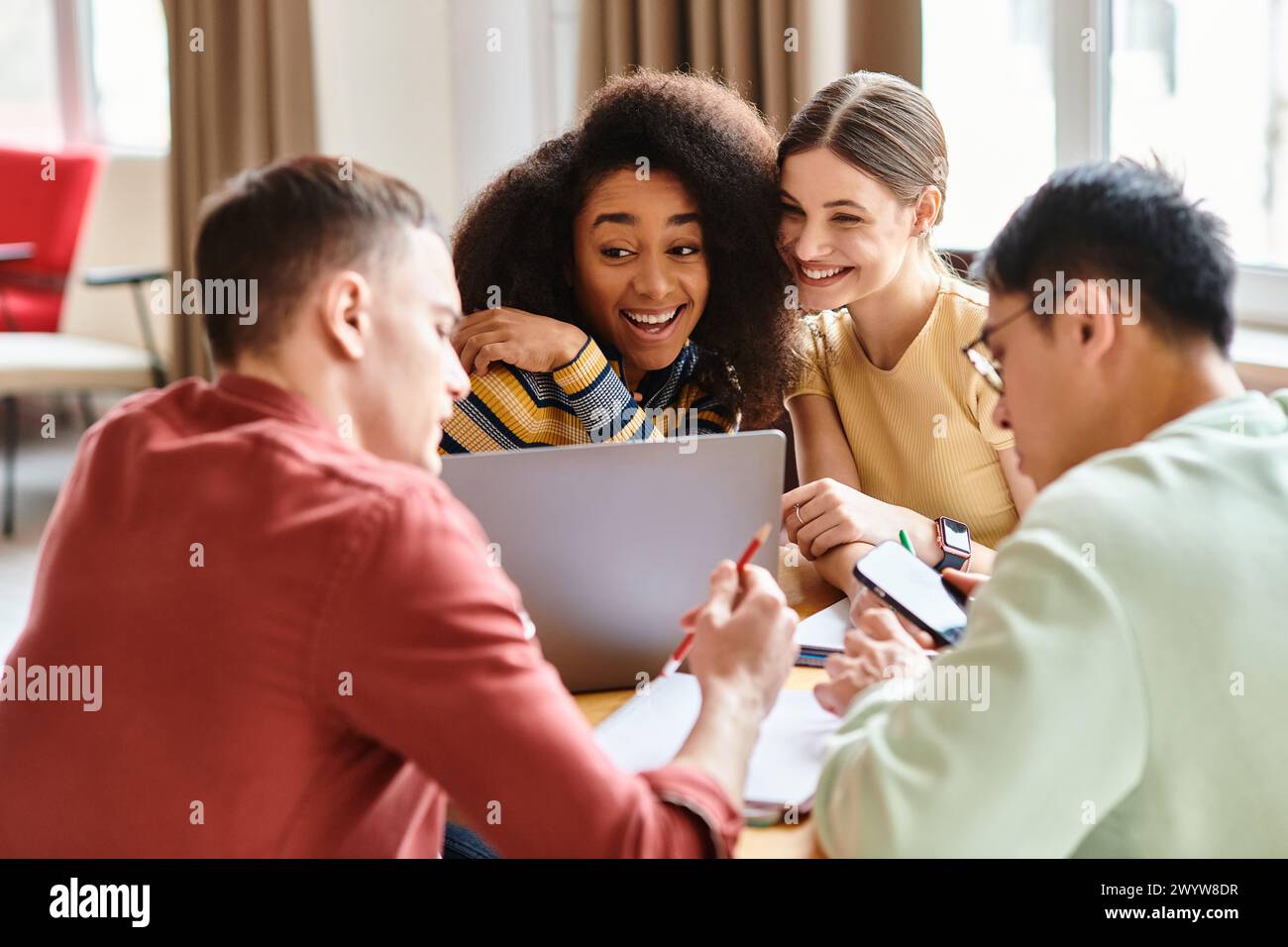 Groupe multiculturel assis autour d'un ordinateur portable, engagé dans la discussion et l ...