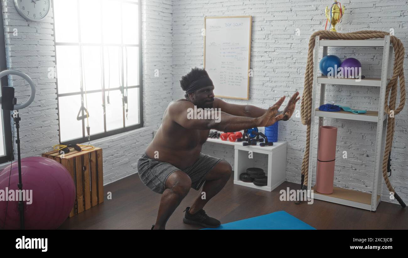 Jeune homme afro-américain faisant des squats dans un gymnase intérieur ...