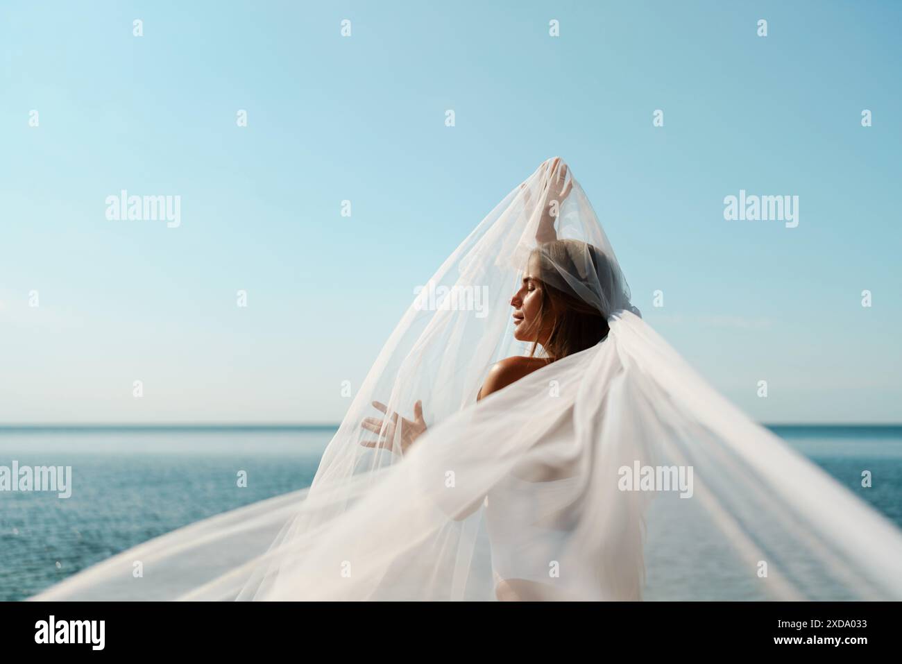 Une femme se tient sur une plage avec un voile blanc sur la tête. La ...