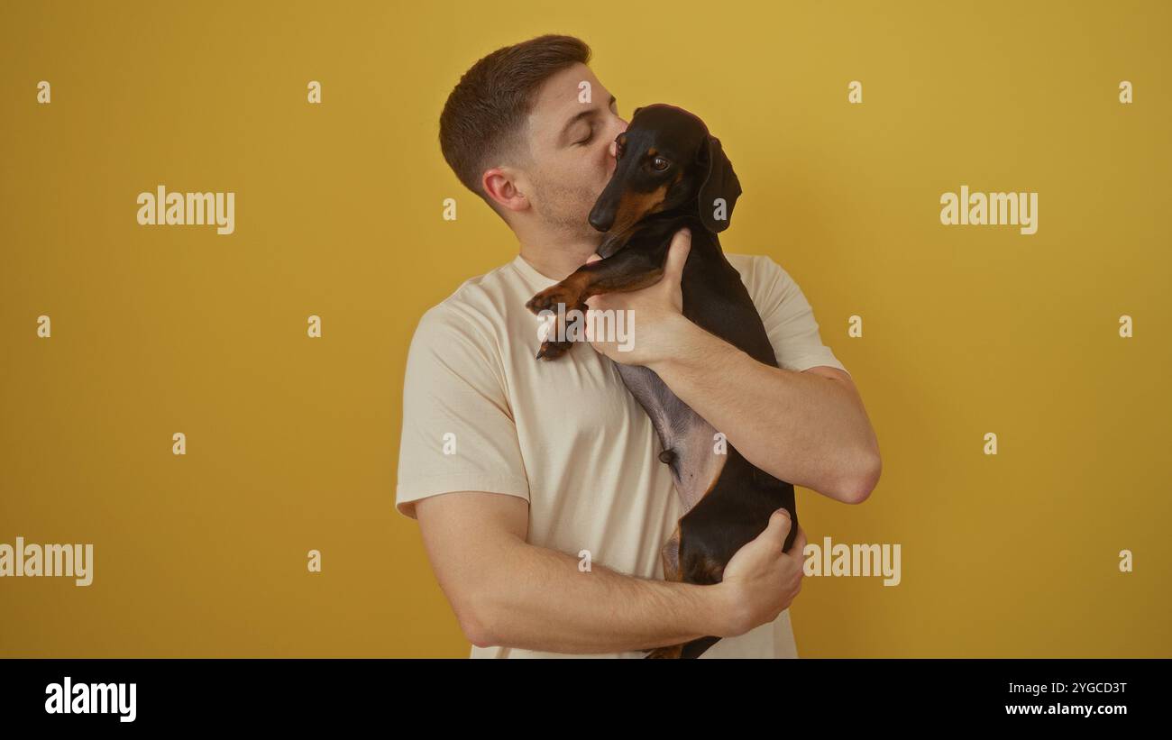 Un jeune homme hispanique embrasse son chien teckel sur un fond jaune ...