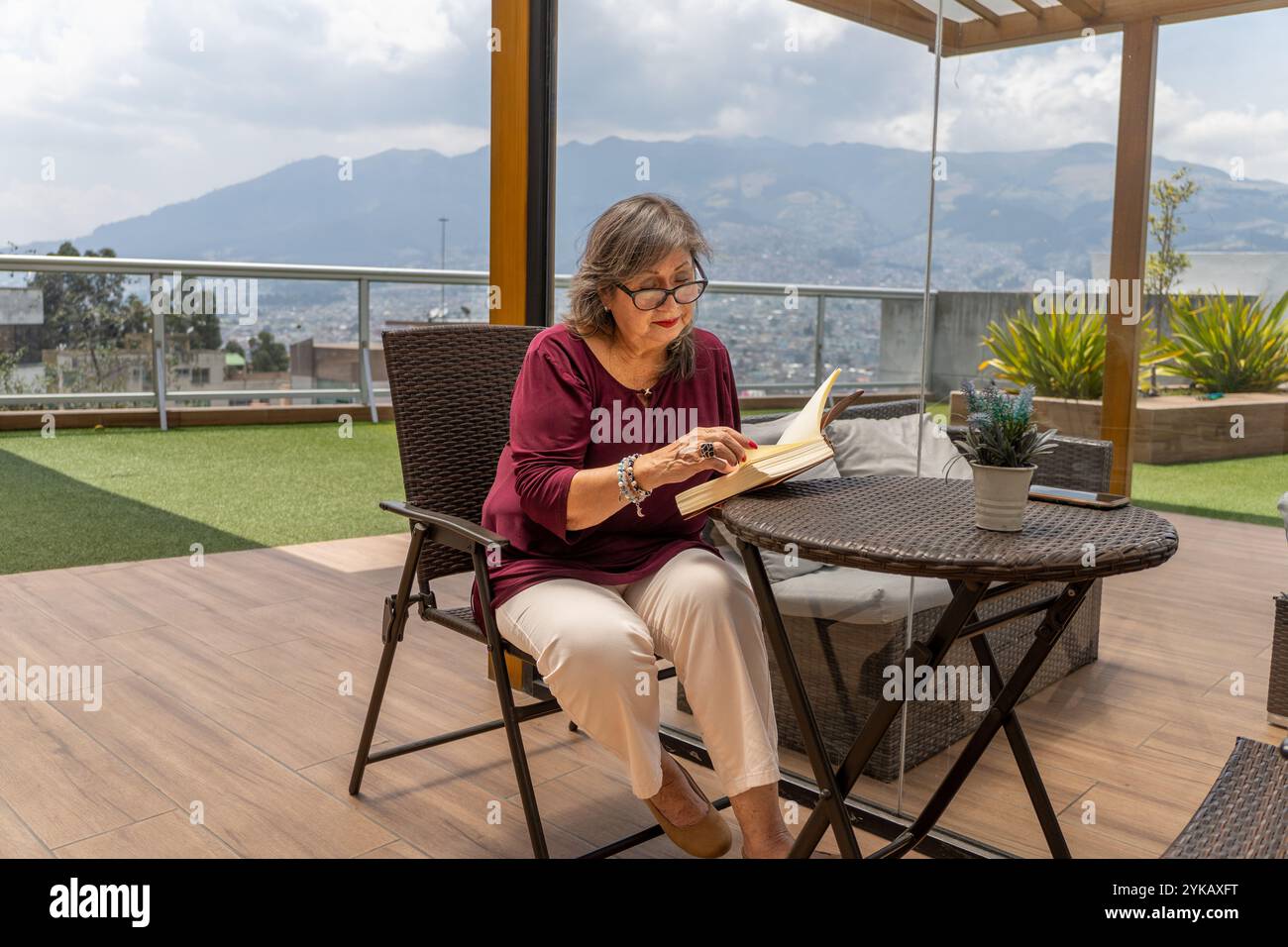 Une femme est assise à une table en train de lire un livre. La scène se déroule dans un jardin ...
