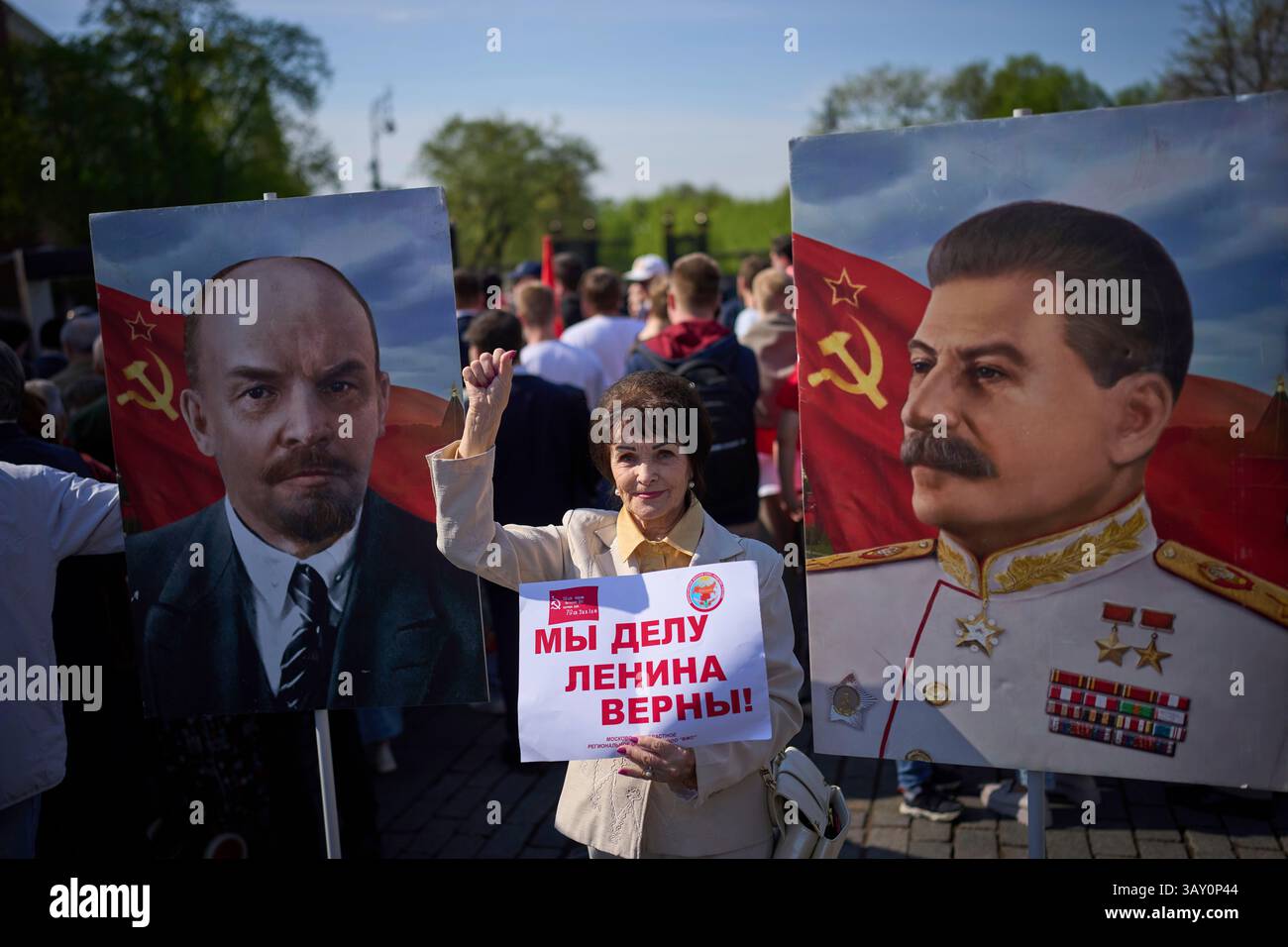 A woman with a poster reads "We're dedicated to Lenin's caus!" poses ...
