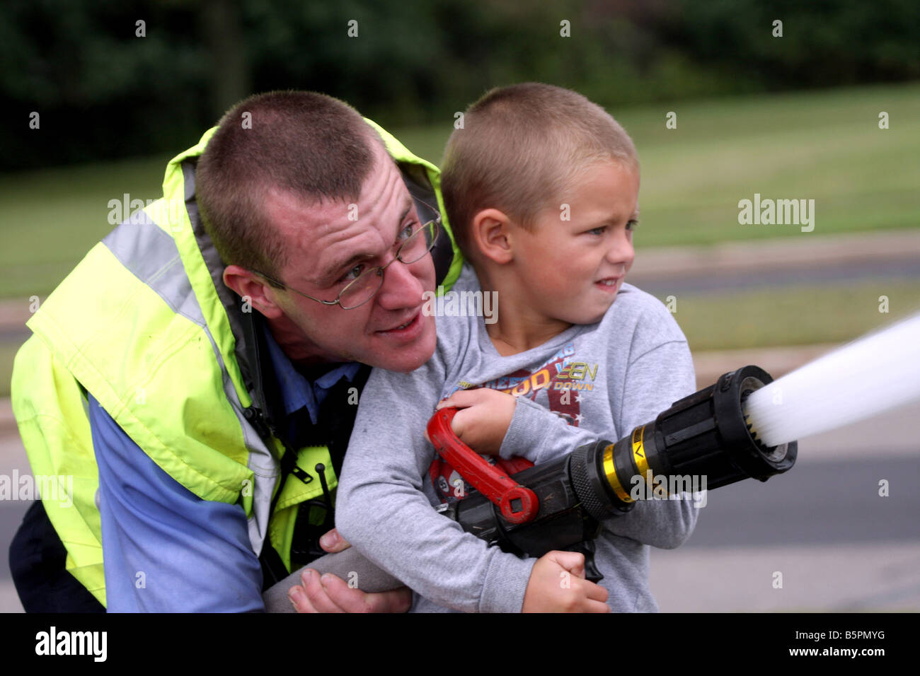 Un pompier aide un jeune garçon utiliser la lance à incendie avec une ...