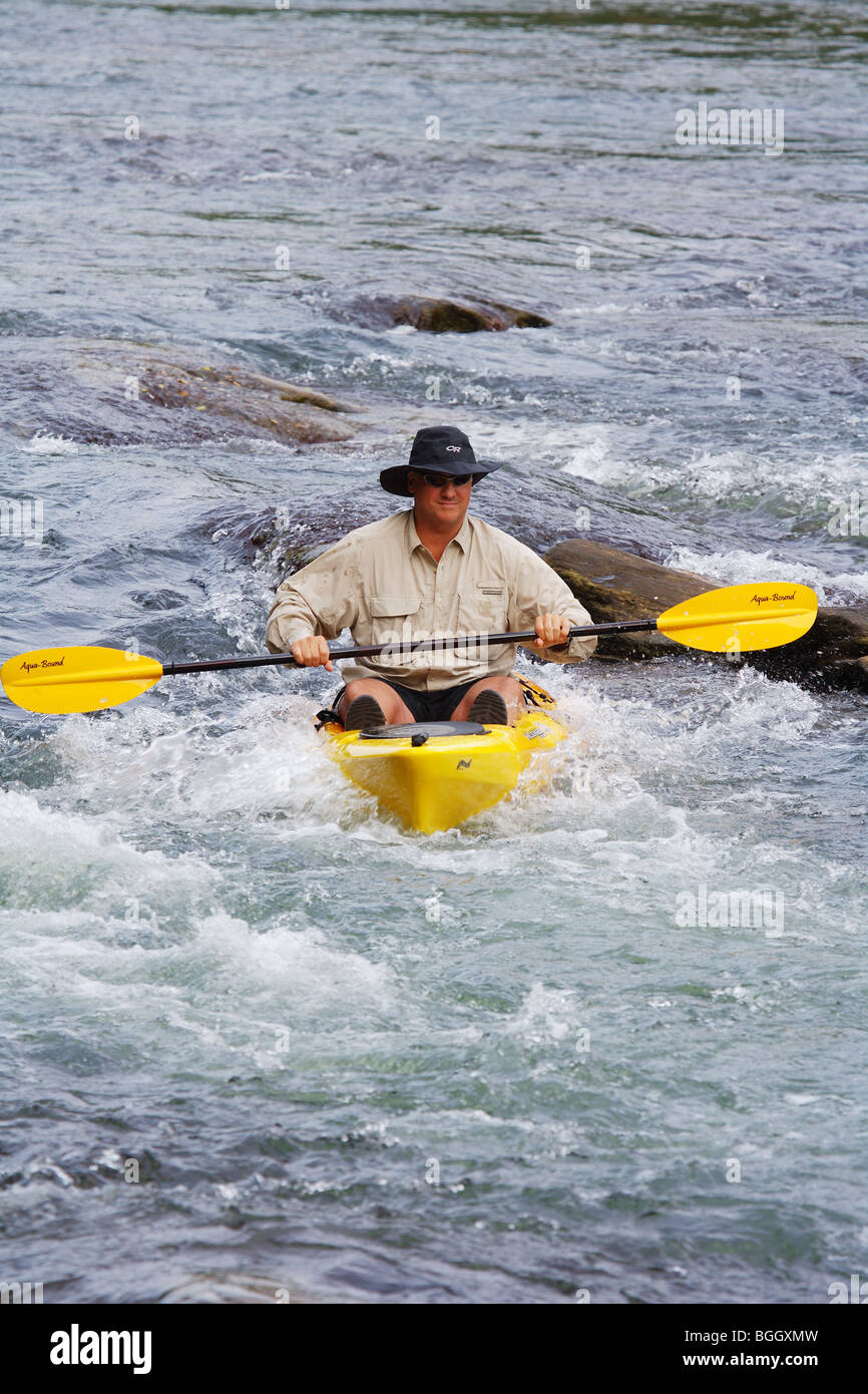 Man paddling à travers des rapides de classe I-II en kayak rivière ...