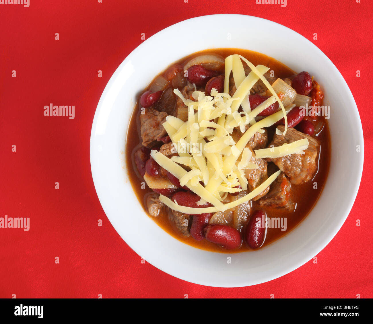 Un bol de chili au bœuf, garni de fromage, sur une nappe rouge avec ...
