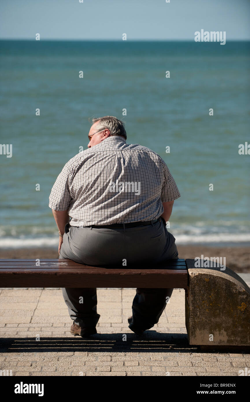 Vue arrière d'un embonpoint homme assis sur un banc en bord de, UK ...