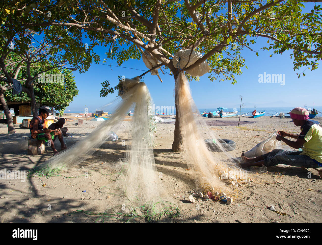 Les hommes réparant leurs filets de pêche sur une plage, à Dili, au ...