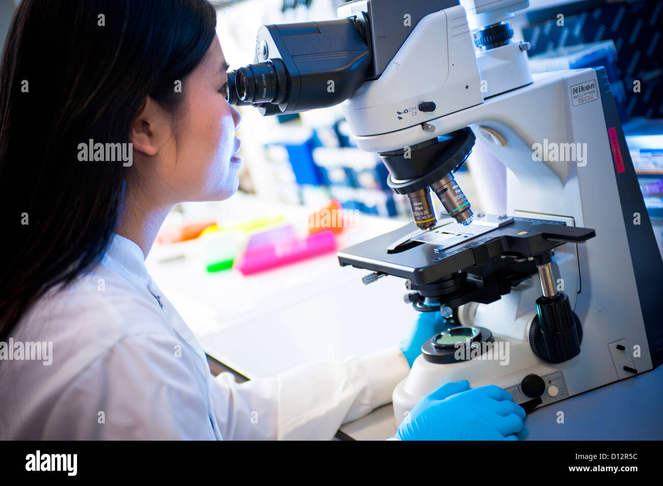 Asian female scientist utilise un microscope pour examiner les cellules ...