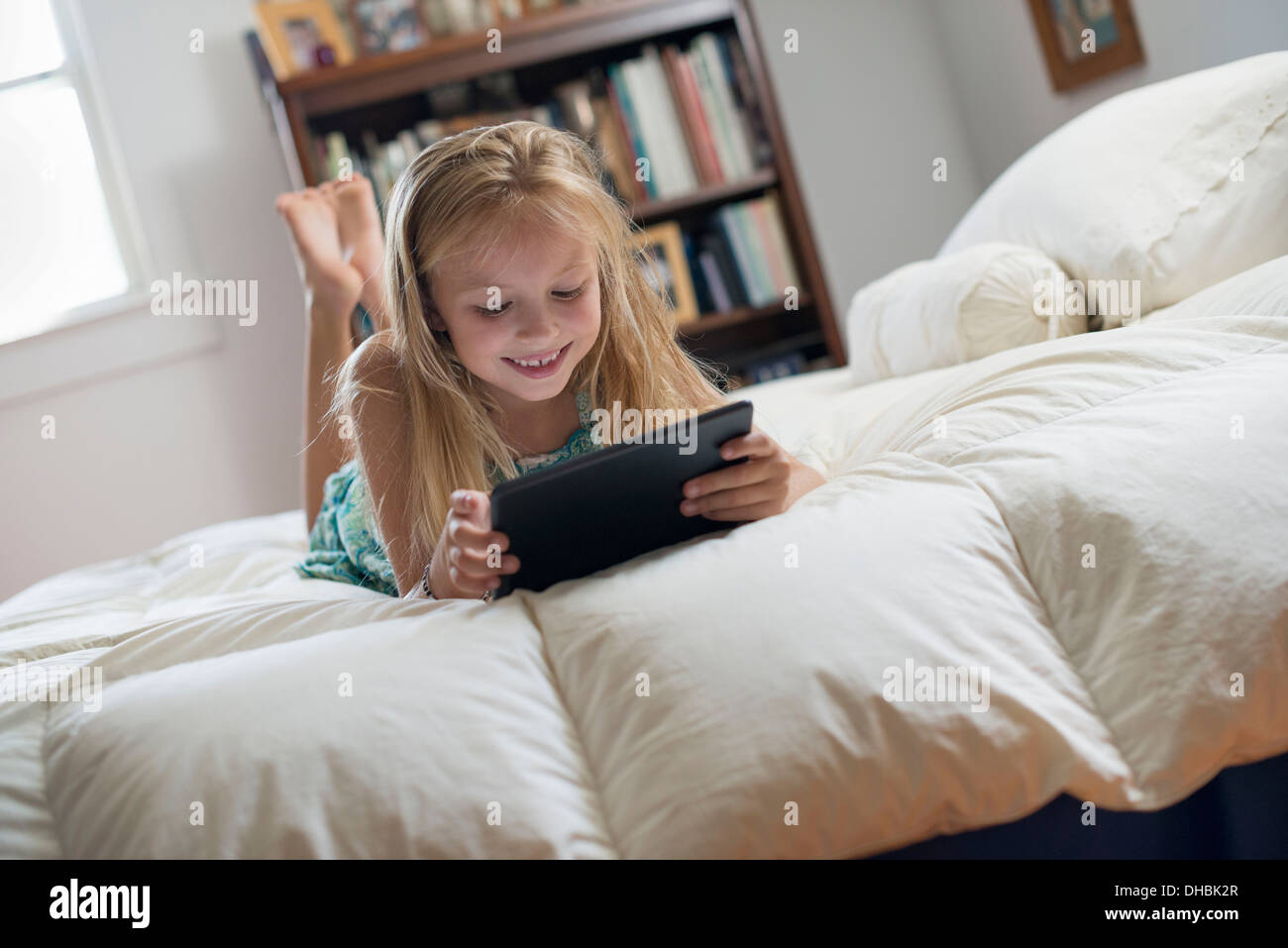 Une jeune fille assise sur son lit à l'aide d'une tablette numérique Photo Stock - Alamy