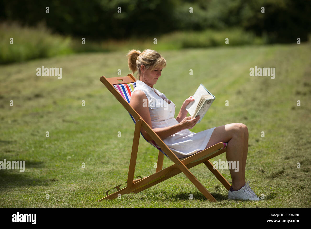 Femme assise dans un livre de lecture de chaise longue Banque de photographies et d’images à ...