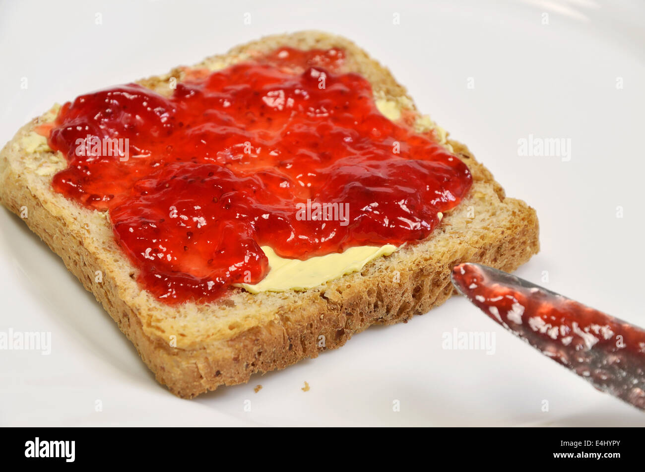 Sandwich de pain grillé avec de la confiture de fraise et beurre sur plaque blanche avec couteau ...