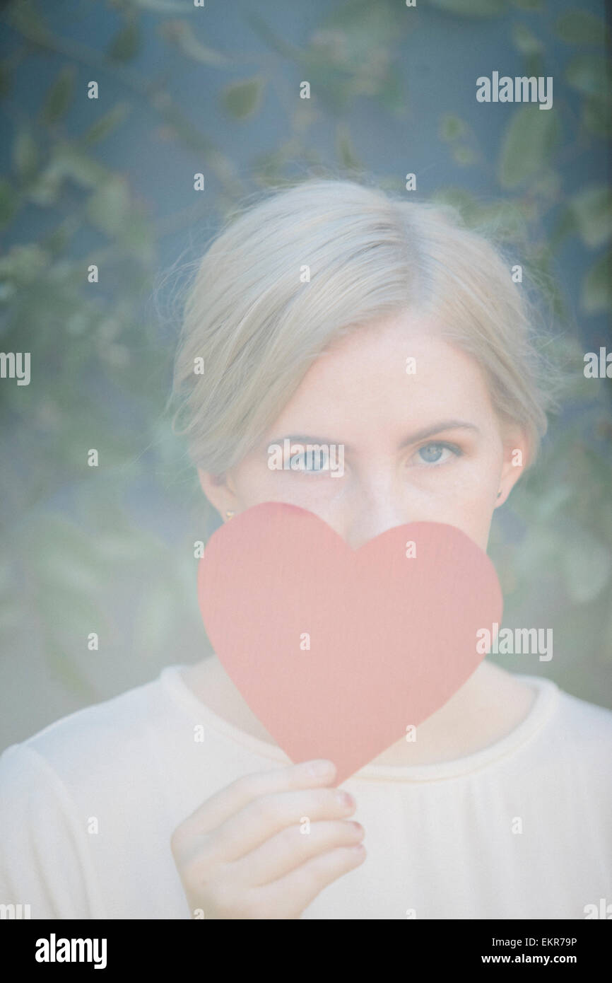 Une femme tenant une forme de coeur rouge en face de son visage Photo ...