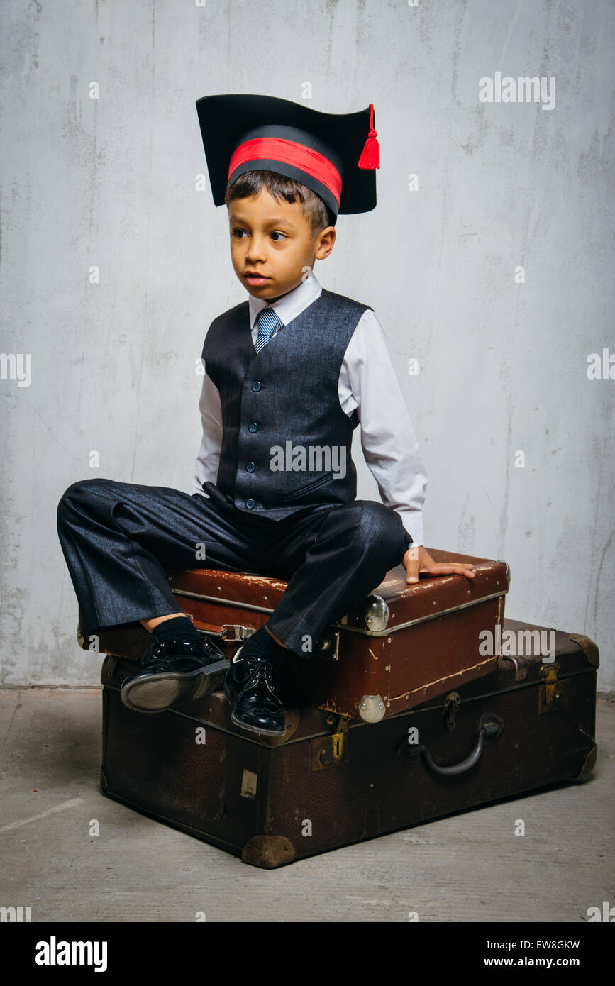 Petit garçon noir en graduation hat se trouve sur l'ancienne valises ...