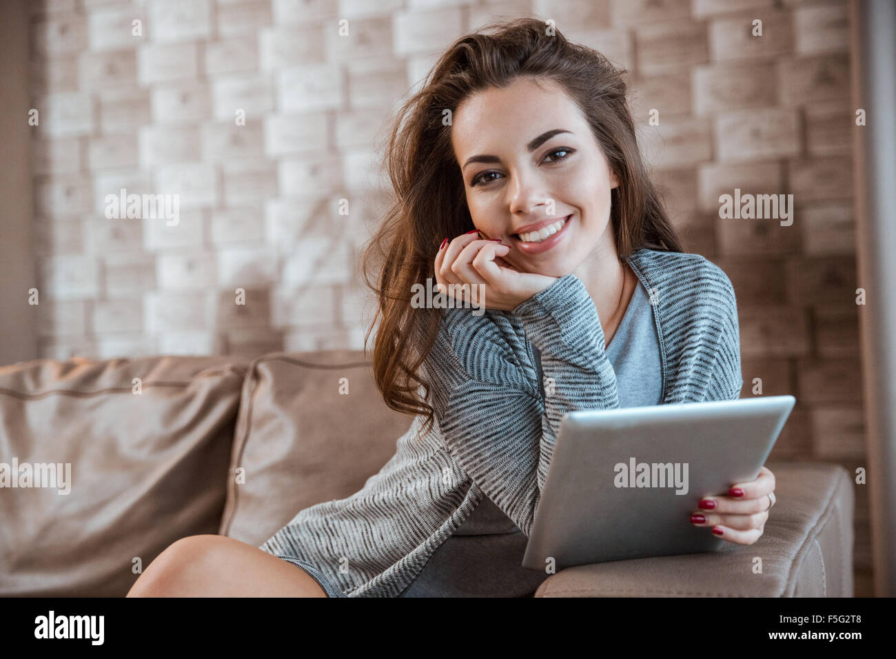 Happy smiling beautiful girl sitting on sofa holding Photo Stock - Alamy
