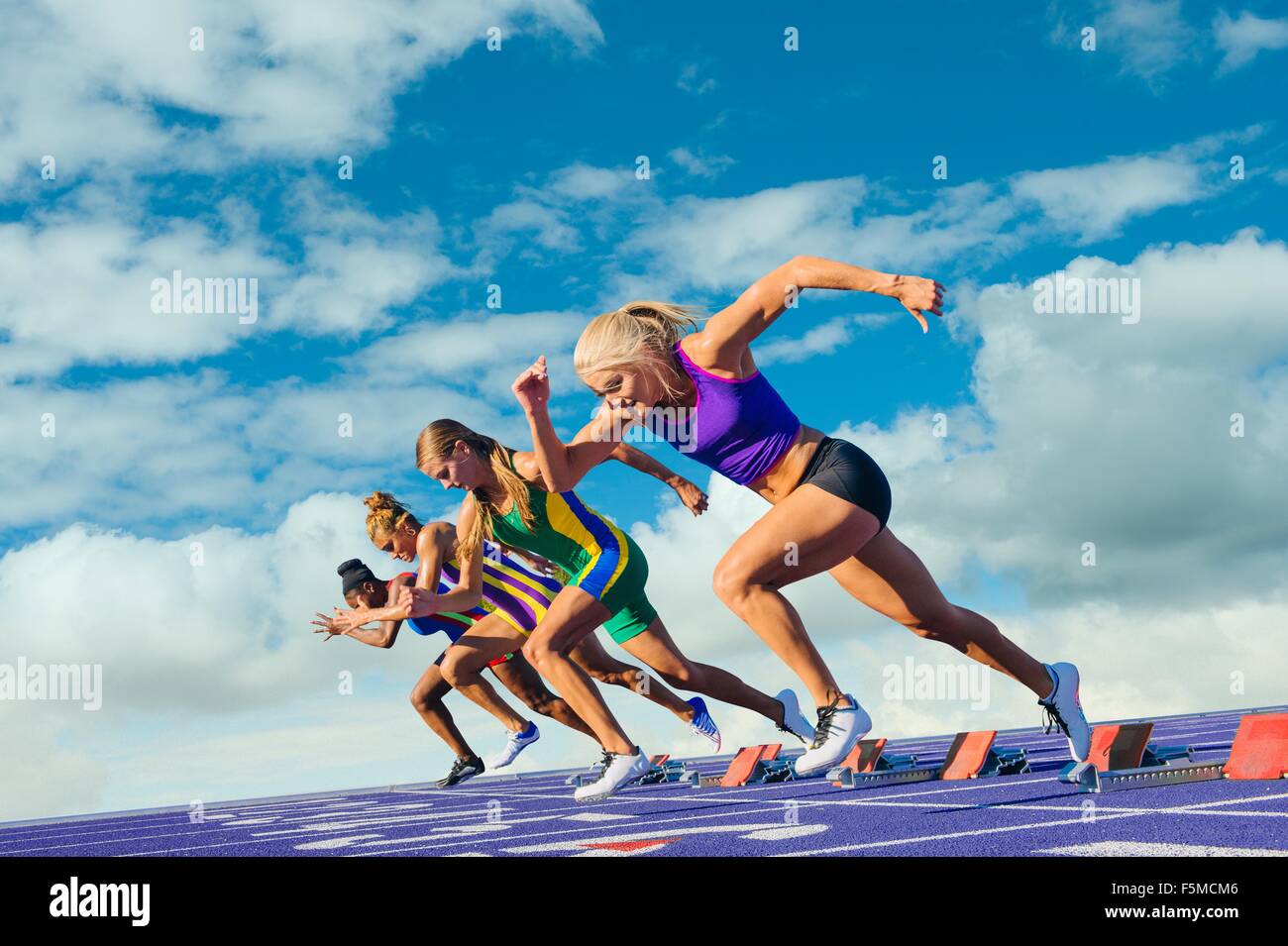 Quatre femmes athlètes sur piste d'athlétisme, laissant starting-blocks ...