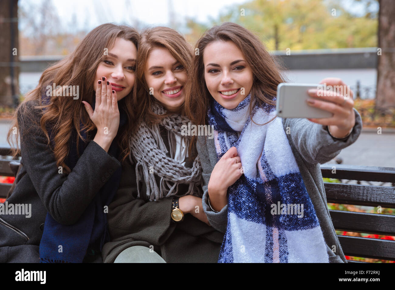 Portrait of a happy trois copines assis sur le banc et de faire sur ...