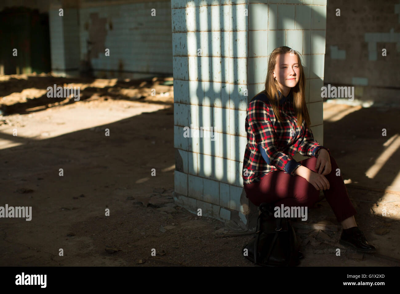 Teen girl sitting dans un bâtiment abandonné dans les rayons de lumière ...