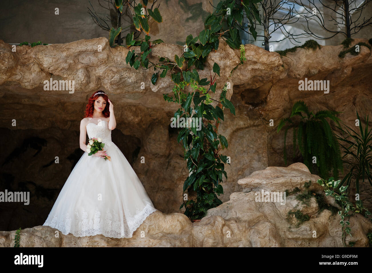 Rousse charmante épouse modèle avec bouquet de mariage à la main posée ...