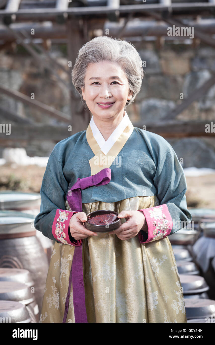 Smiling old woman in traditional Korean clothes holding pâte de piment ...