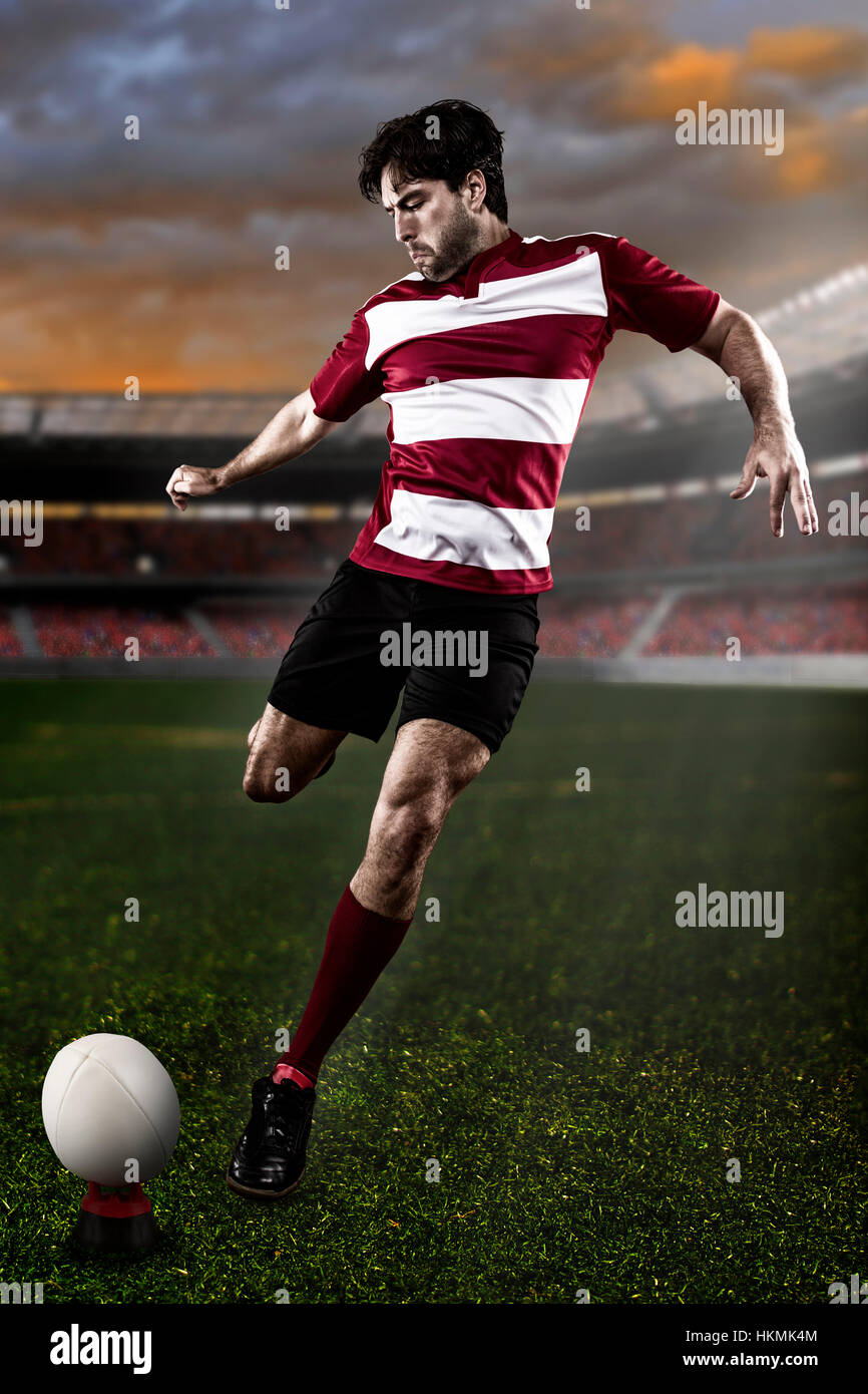 Joueur de Rugby dans un uniforme rouge botter un ballon sur le stade ...