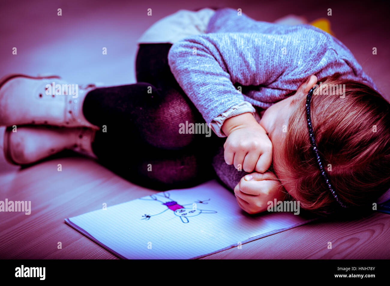 Bouleversée petite fille recroquevillée sur le lit à côté de son dessin ...