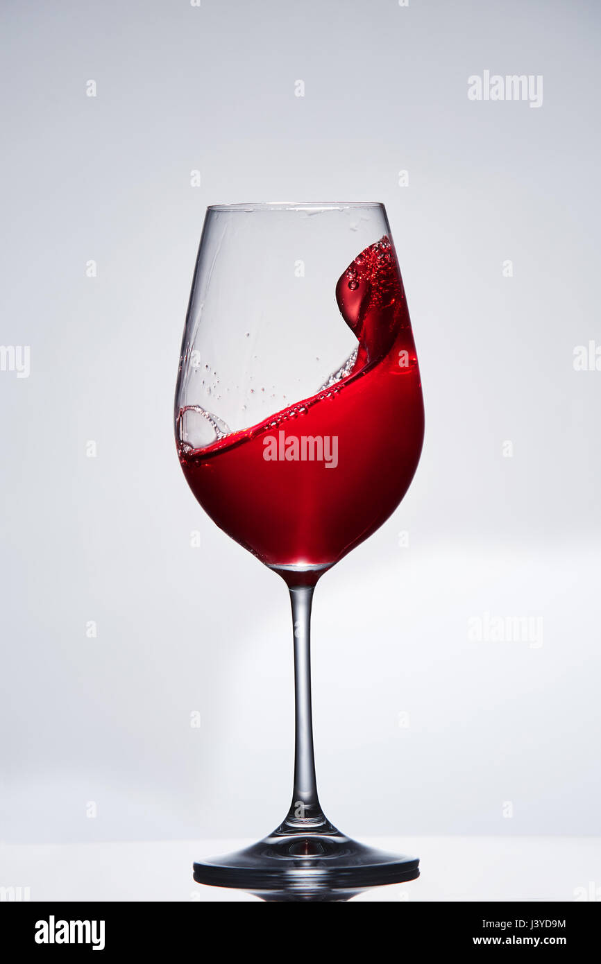 Vin rouge splash dans le délicat verre élégant contre permanent fond ...